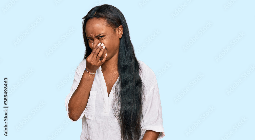 Young black woman wearing casual clothes smelling something stinky and ...