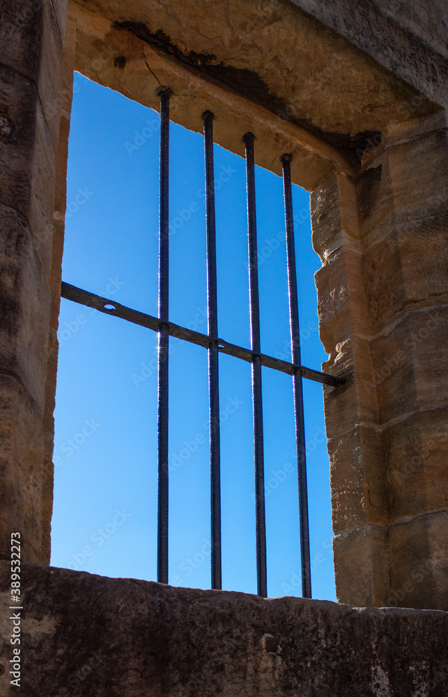 Old sandstone gaol cell (jail cell) with one missing window bar against ...