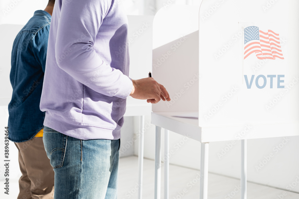 cropped view of multicultural men in polling booth with american flag ...