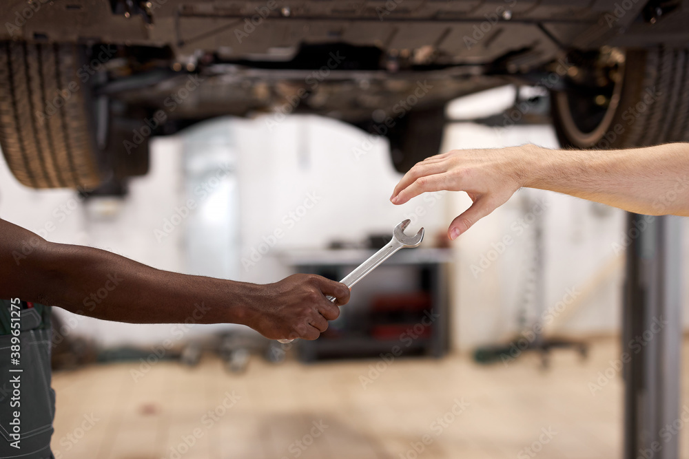 two auto mechnic colleagues giving instrument tools to each other ...