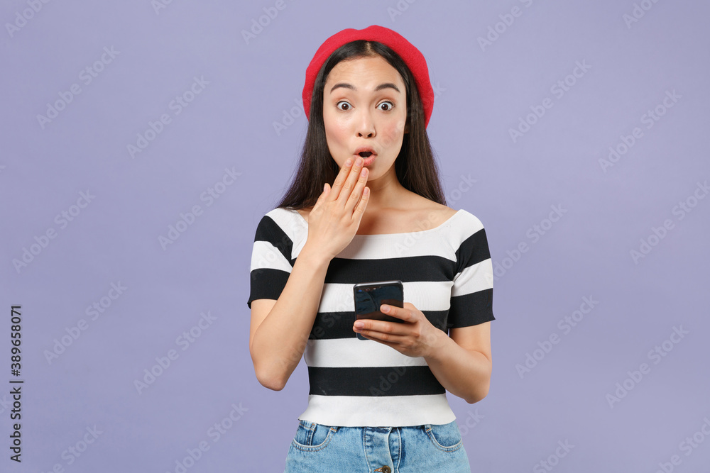 Shocked young asian woman 20s wearing striped t-shirt red beret using mobile cell phone typing ...