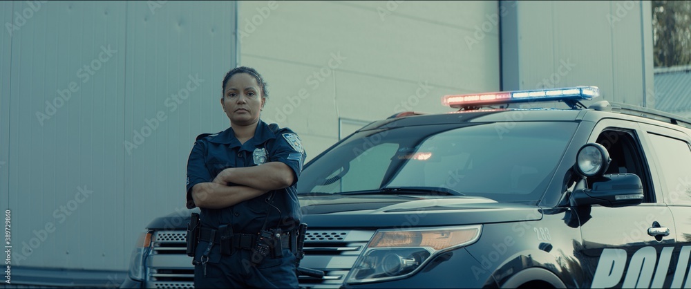 Mixed race female police officer posing against police car with ...