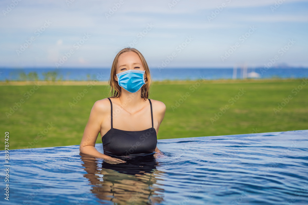 Woman relaxing in infinity swimming pool wearing a medical mask during ...
