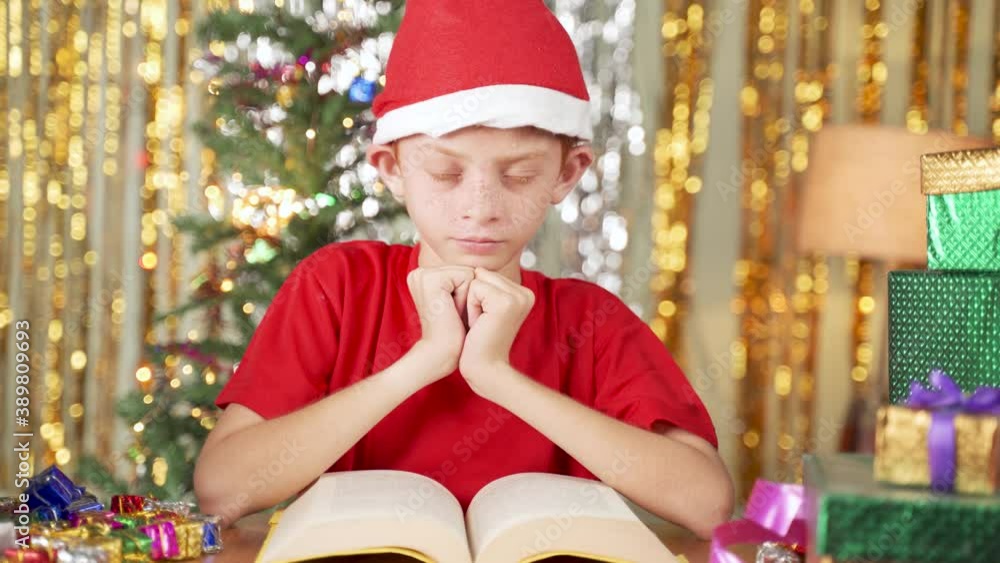 Kid with red Santa hat praying in front of Bible on Christmas decorated ...