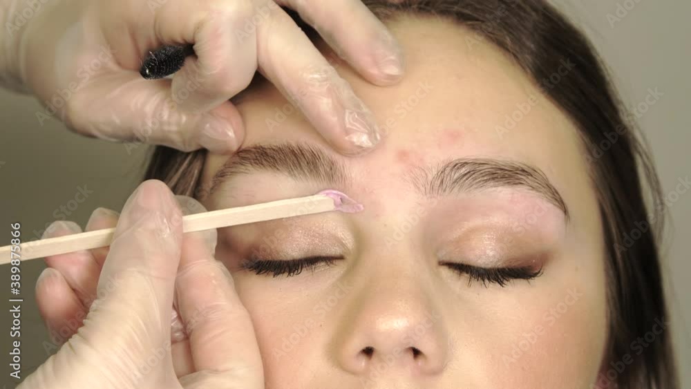Brow master applying wax on the eyebrow of female face of a brunette ...