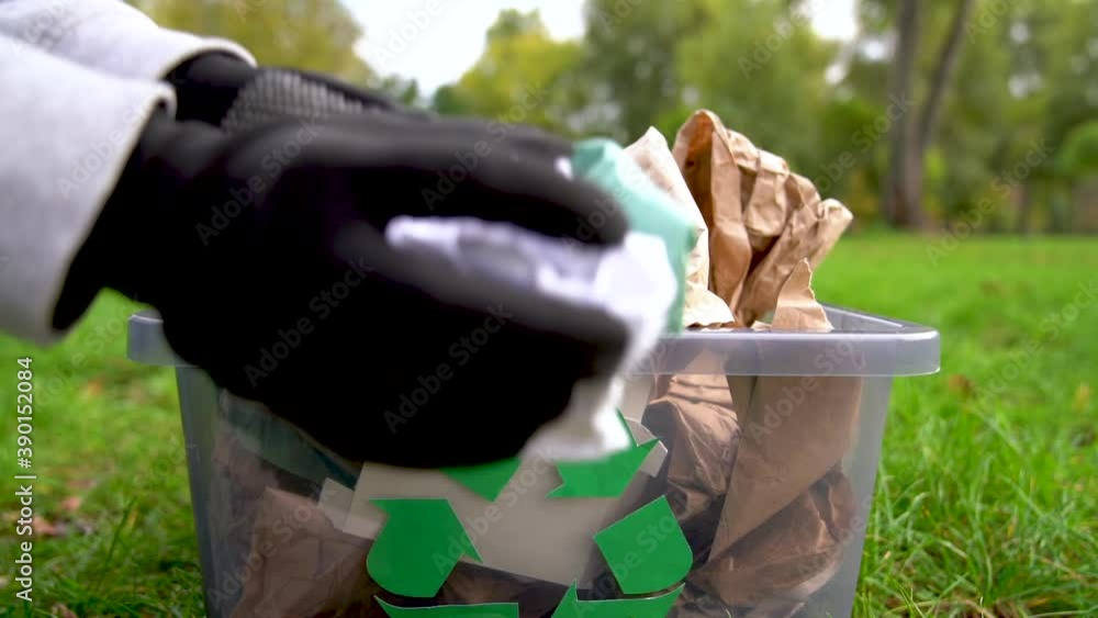 Hand picking up paper trash from grass and put it in box with recycle ...