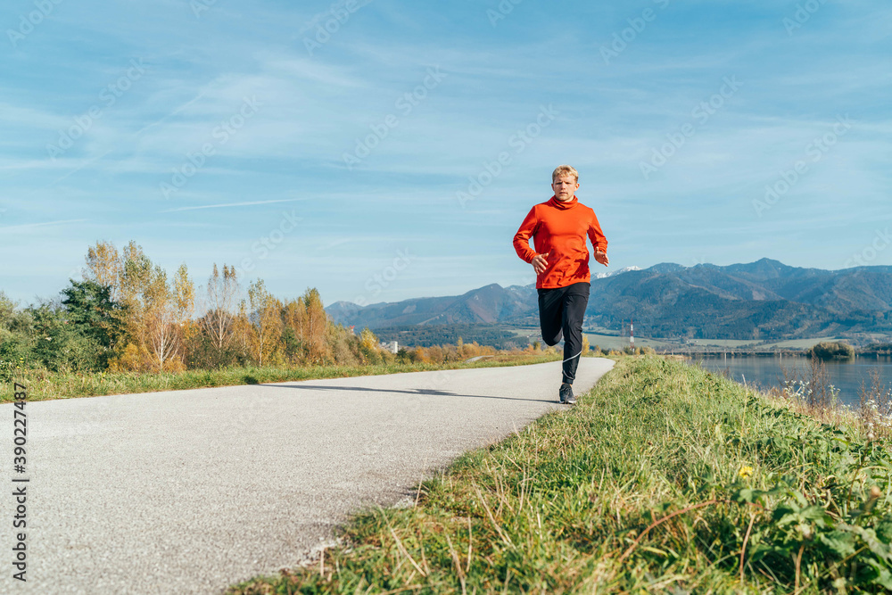 Man dressed in red long sleeve shirt running by the asphalt road with ...