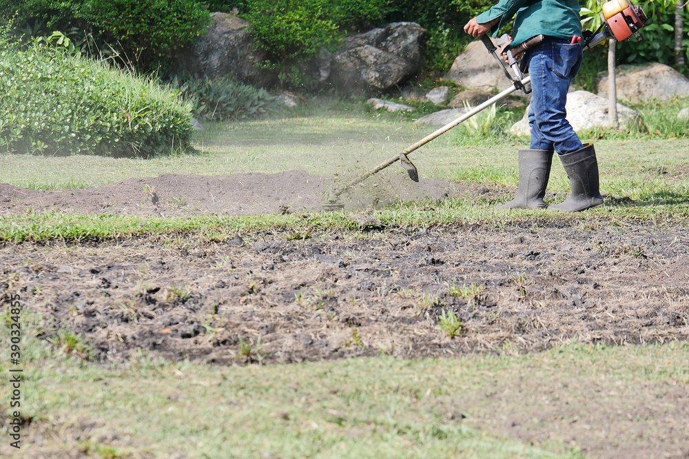 gardener use handheld grass cutter to trim grass in field and soil ...