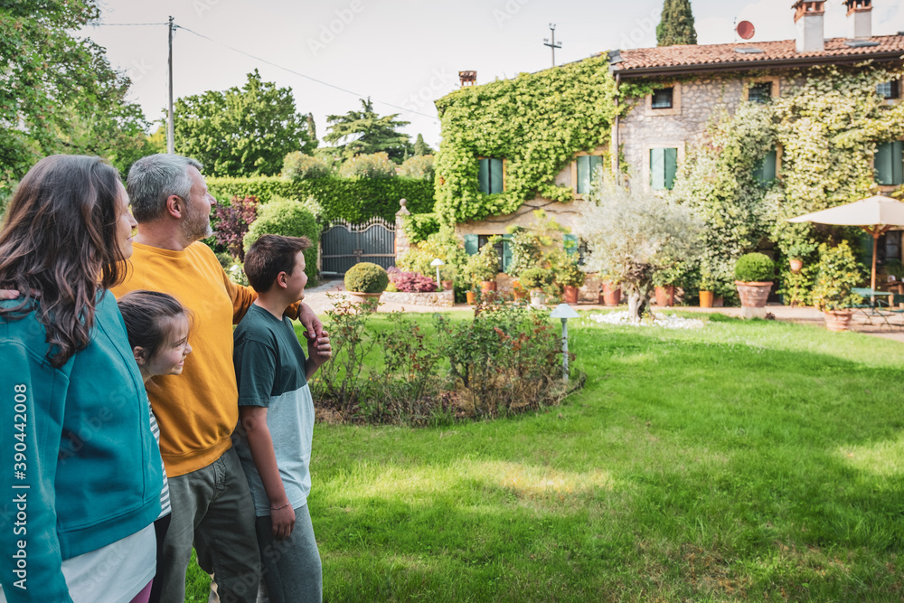 Back view of happy family hugging is standing outside their new house ...
