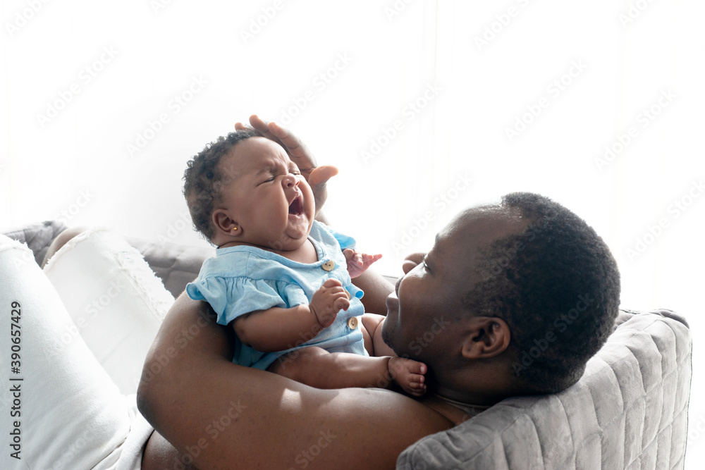Foto de Dark skinned father lying on couch holds his baby daughter in ...