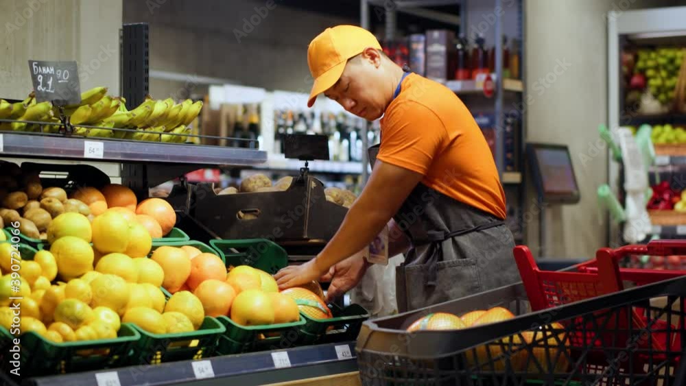 Chinese retail store worker in orange uniform arranging fresh fruits in ...