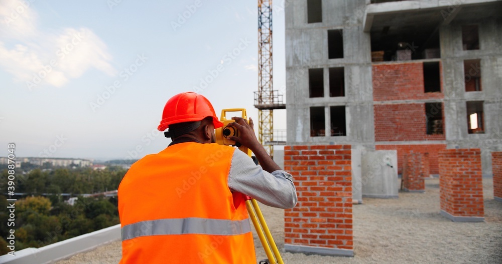 African American young man topographer in casque measuring angle with ...
