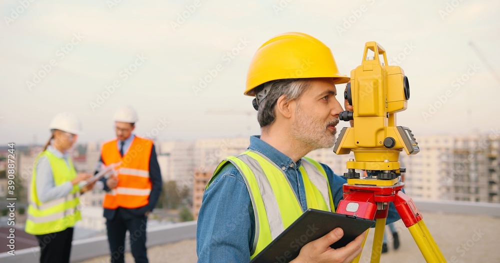 Caucasian man topographer in casque measuring angle with total station ...