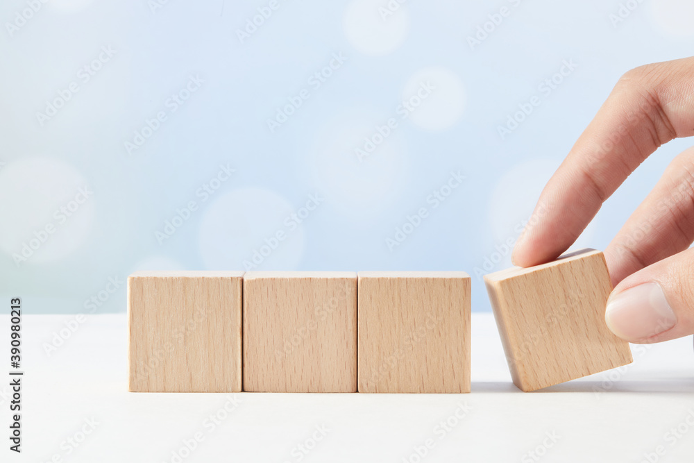 Hand adding one blank wooden block to a row of three wooden blocks ...
