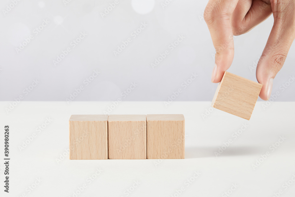 Hand adding one blank wooden block to a row of three wooden blocks ...