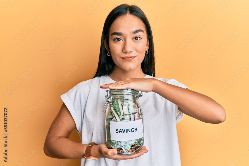 Young asian woman holding jar with savings relaxed with serious ...