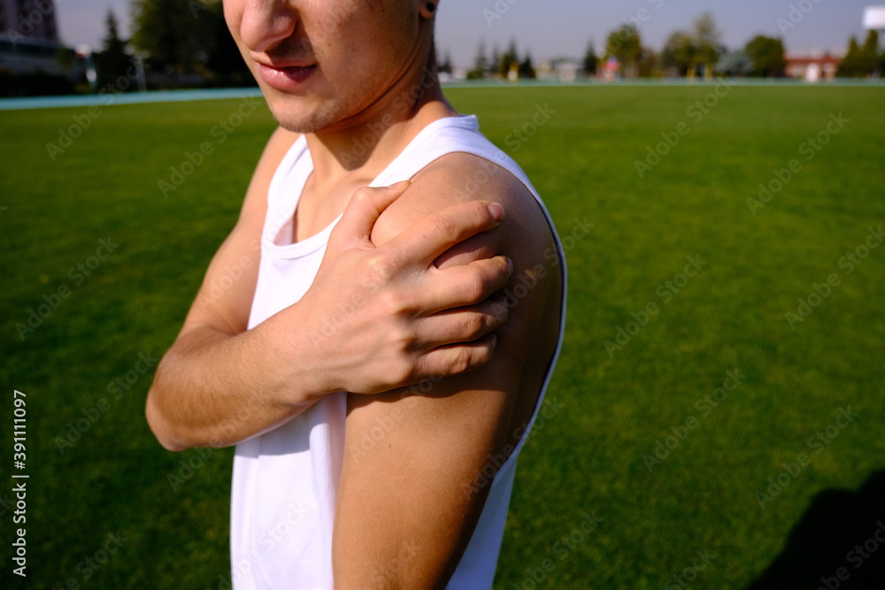 sportsman with shoulder dislocation in turf/sports field, holding his ...