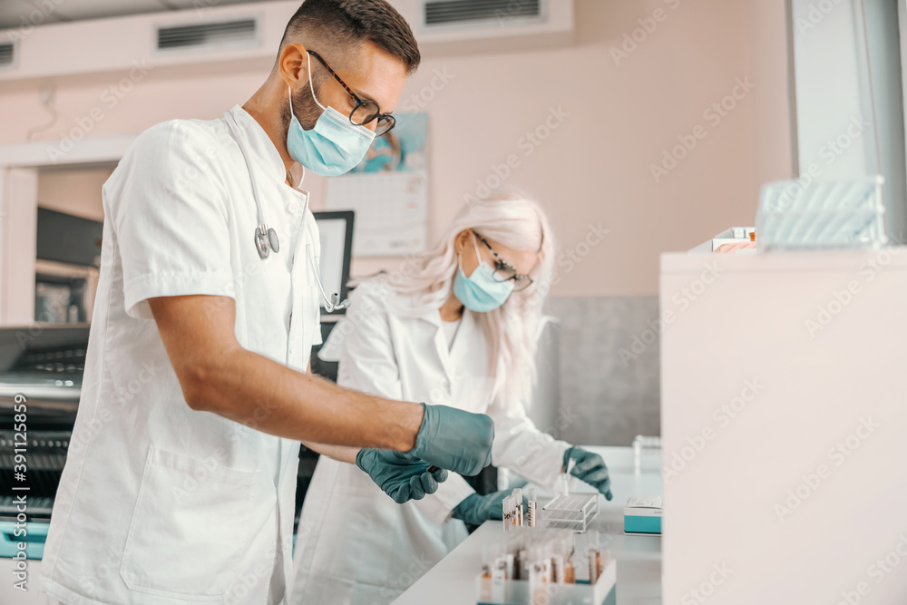 Two focused scientists with rubber gloves and face masks holding test ...