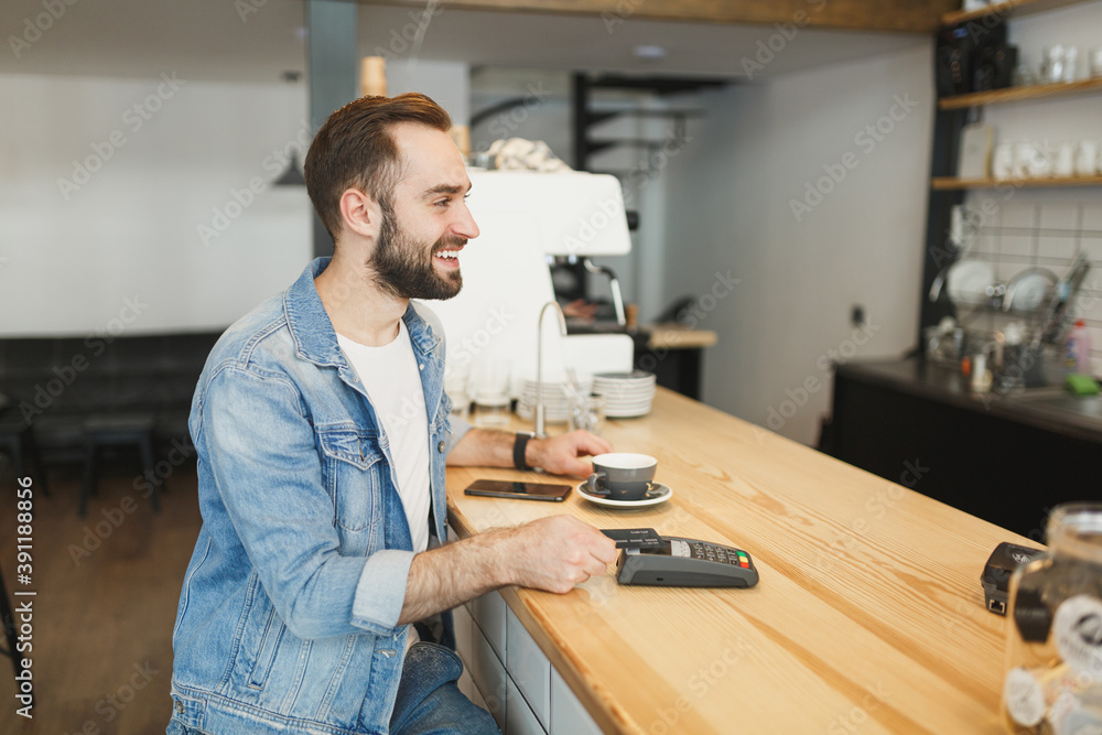 Handsome young man sit in coffee shop cafe hold cup coffee tea pay off ...
