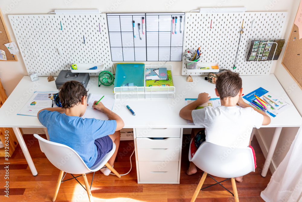 Two boys studying and doing homework sitting in at their desk at home ...