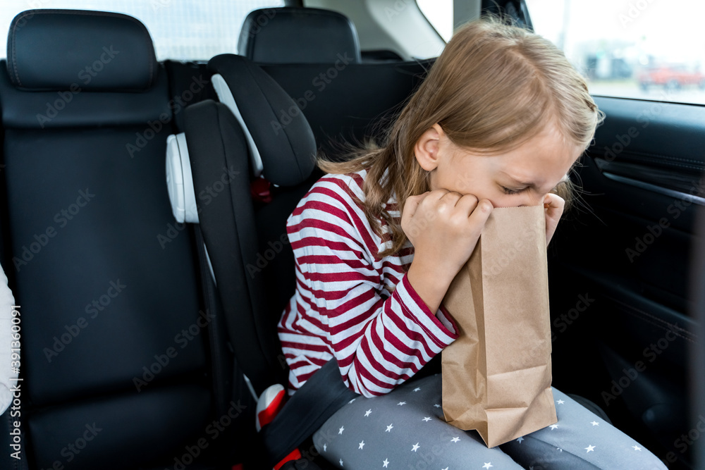 Little girl is driving in car. Kid is sick, feels bad and vomiting into ...