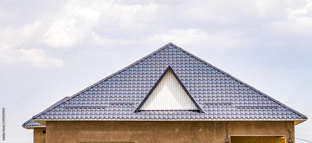 The roof of a house made of metal profile against a blue sky with white ...
