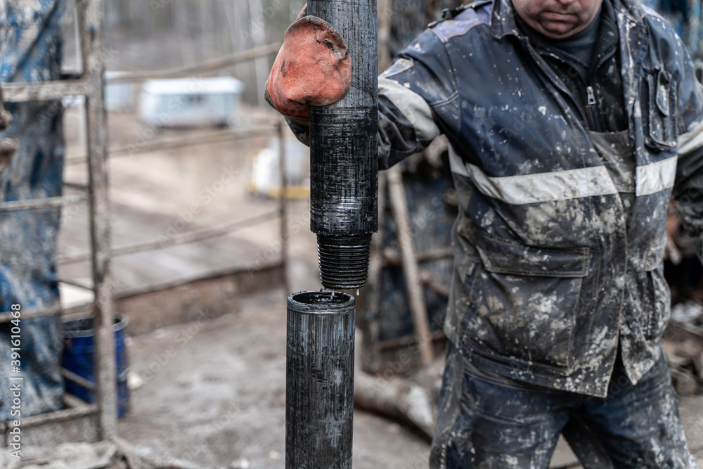 Work driller in red uniform, in helmet and goggles. He uses a hydraulic ...