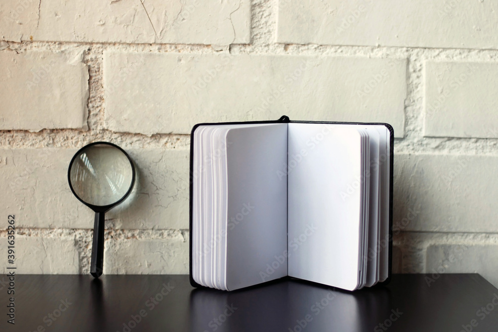 Magnifying glass next to a black notebook. Stock Photo | Adobe Stock