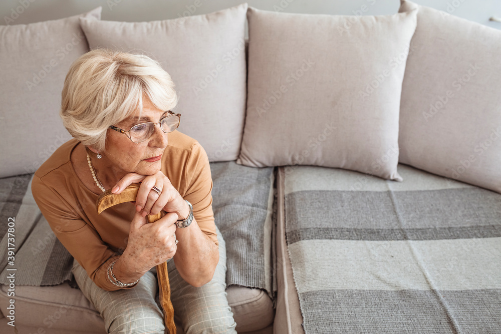 Senior Woman Sitting On Sofa And Holding Walking Stick Alone