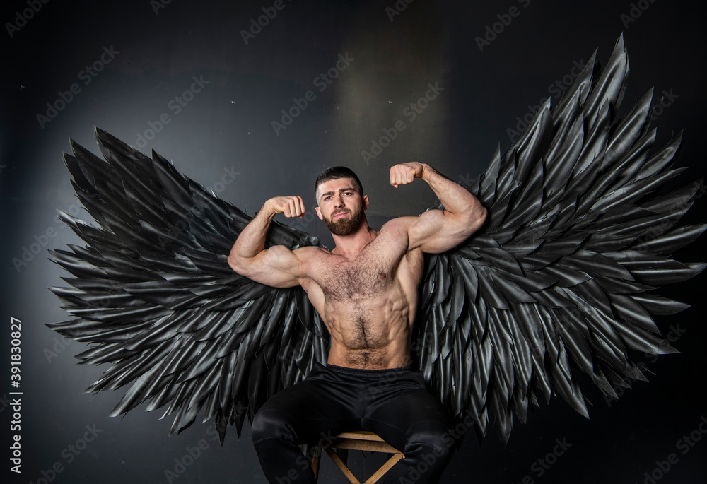 handsome physically well-developed man with black angel wings on a dark ...