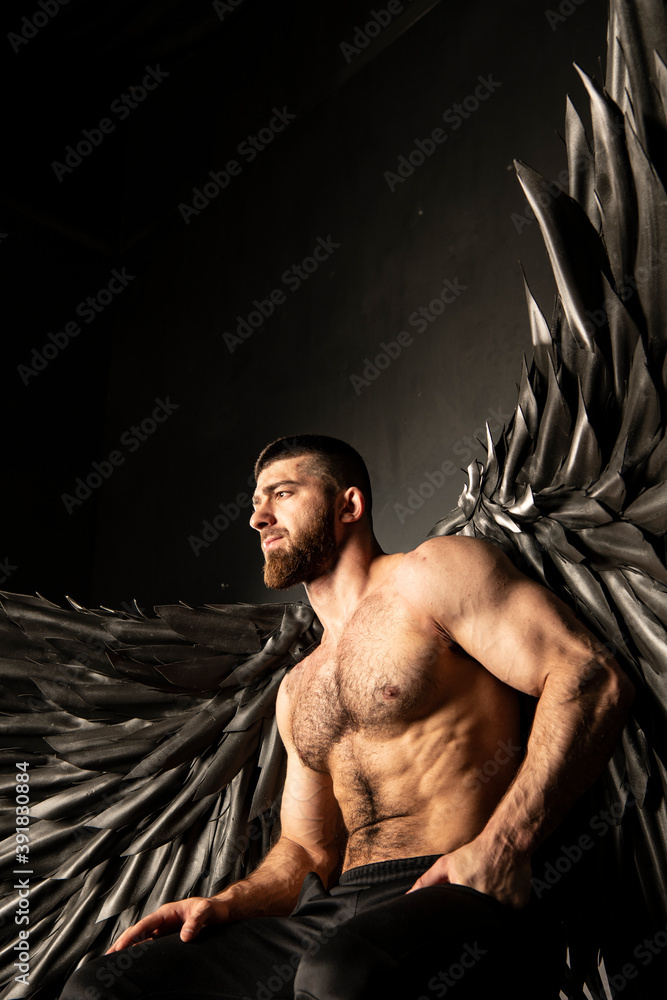 handsome physically well-developed man with black angel wings on a dark ...