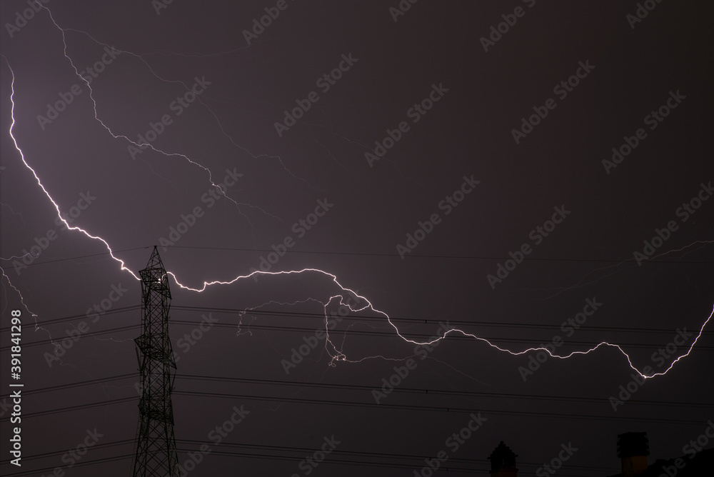 A giant thunderstorm flashes through a high voltage pylon and touches ...