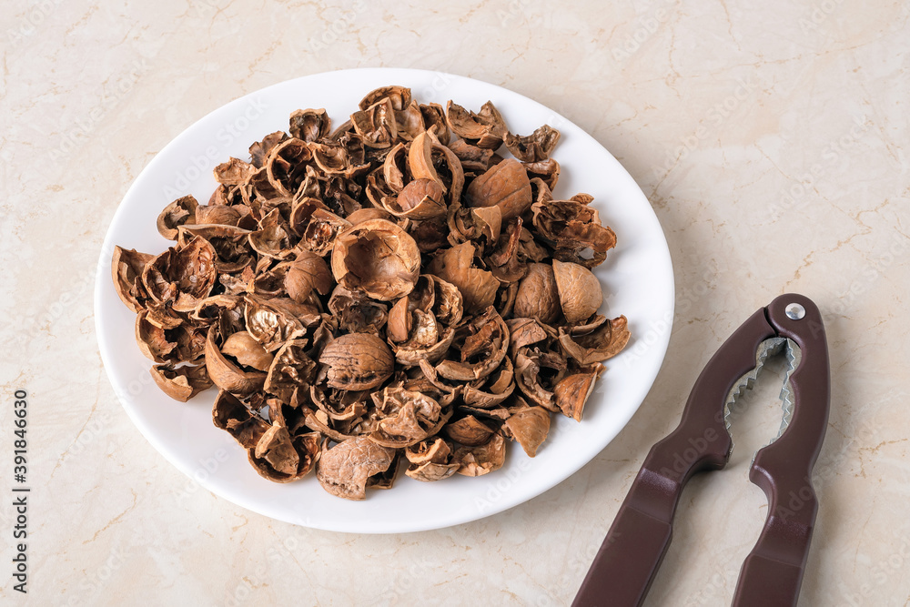 Pile of empty broken walnut shells on a white plate and nutcracker over ...