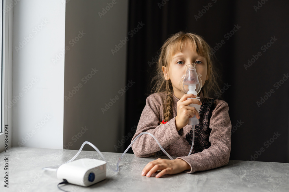 Little girl makes inhalation with a nebulizer at home, sitting on a ...