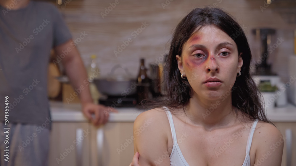 Portrait of hopeless beaten woman sitting on the chair in the kitchen. Traumatised abused ...