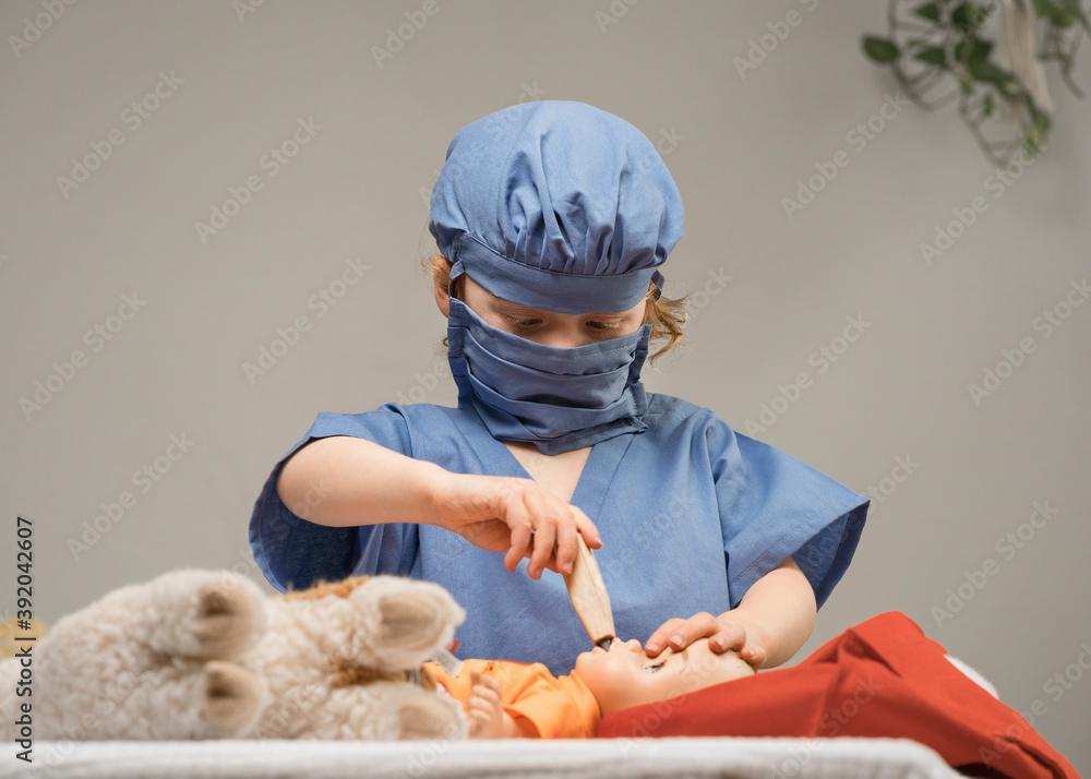 young child wearing medical PPE examines a baby doll by checking it's ...