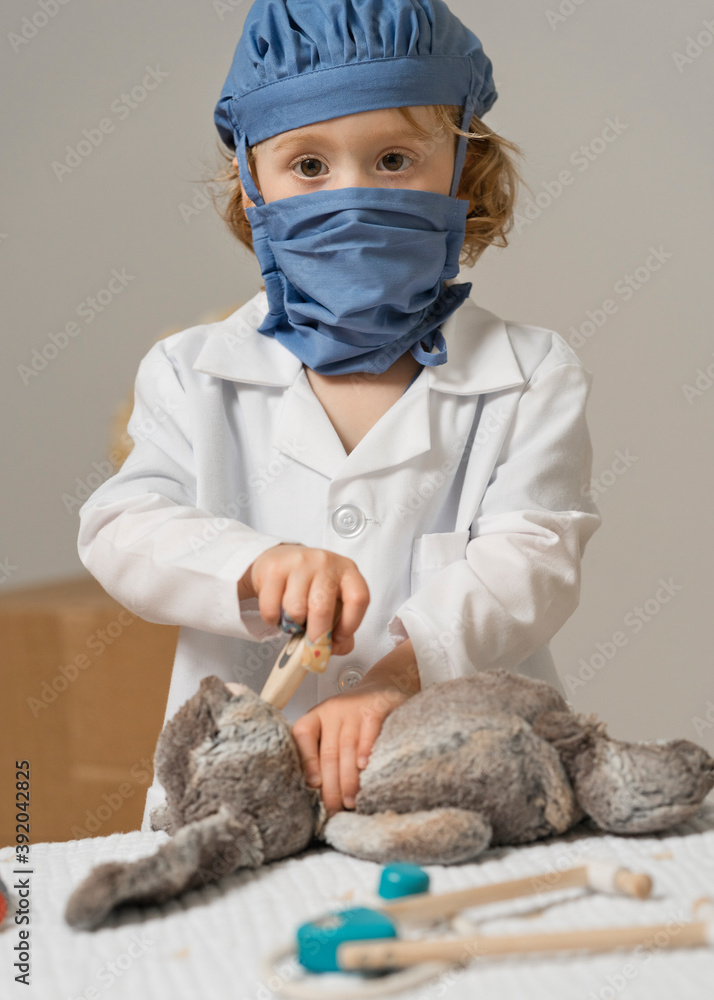young child in medical PPE examines a plush toy rabbit by taking it's ...