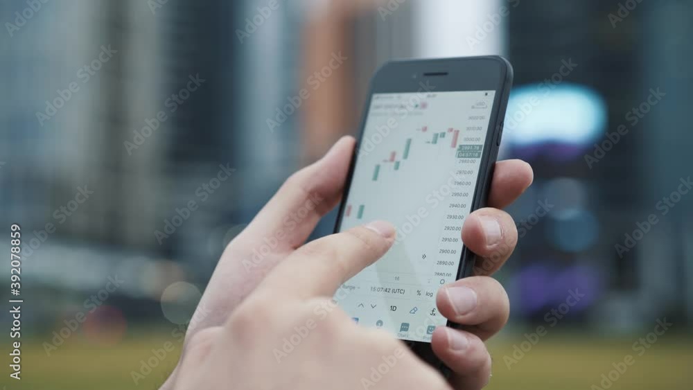 Hands with a mobile phone, checking stock market data on background of ...