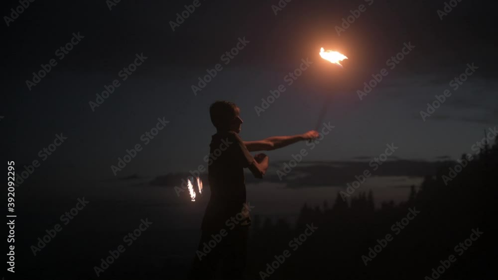 Graceful male fireshow performer making fire dance with two metal fans ...