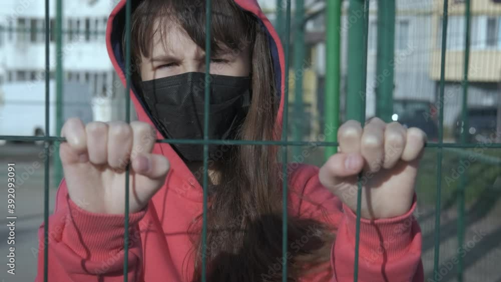 Restriction due to coronavirus. A sad child in medical mask hold bars ...