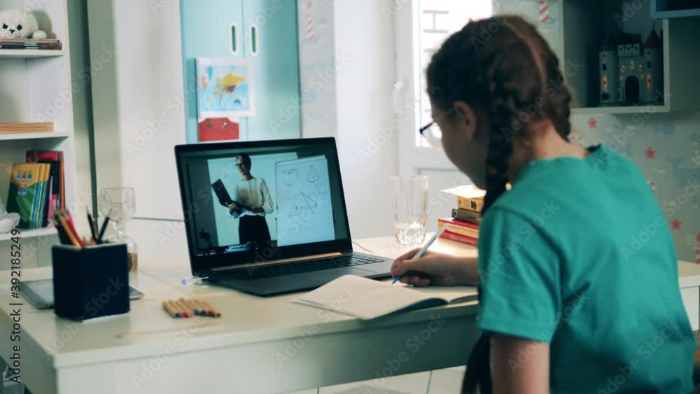 Schoolgirl studying remotely at home using a laptop. Remote education ...