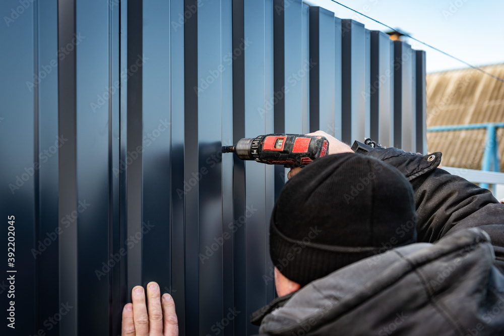 Metal fence installation. The worker is screwing the screw into the ...