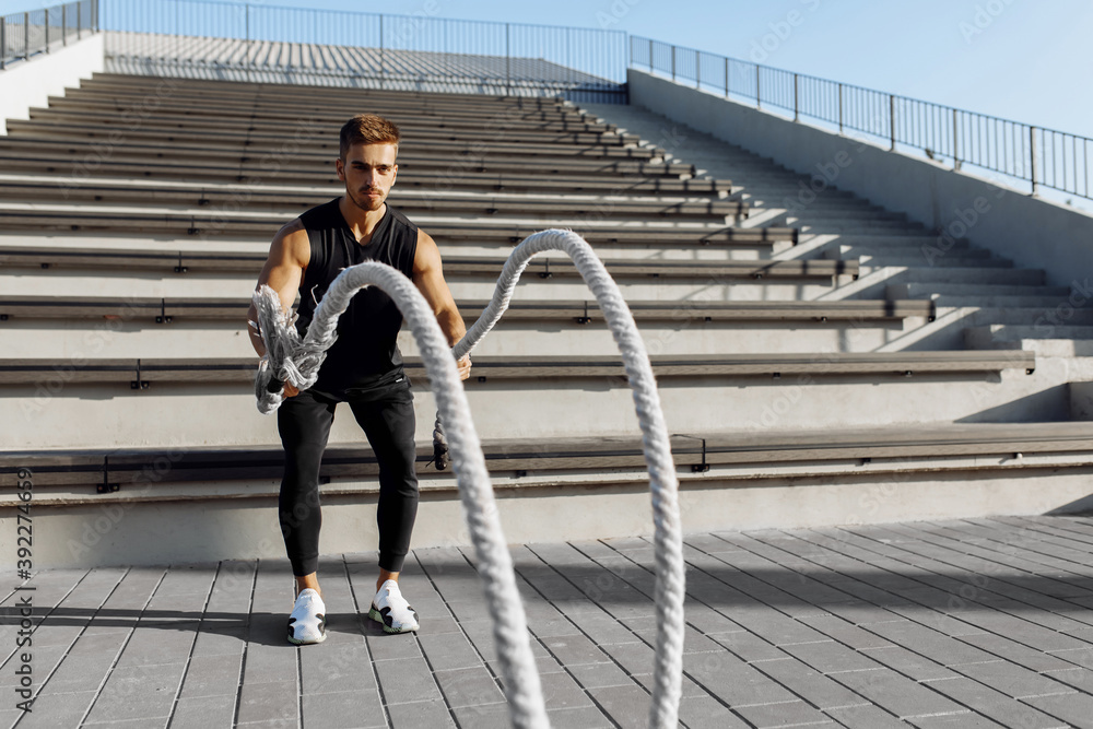 Strong young man exercising with crossfit fighting ropes, muscular ...