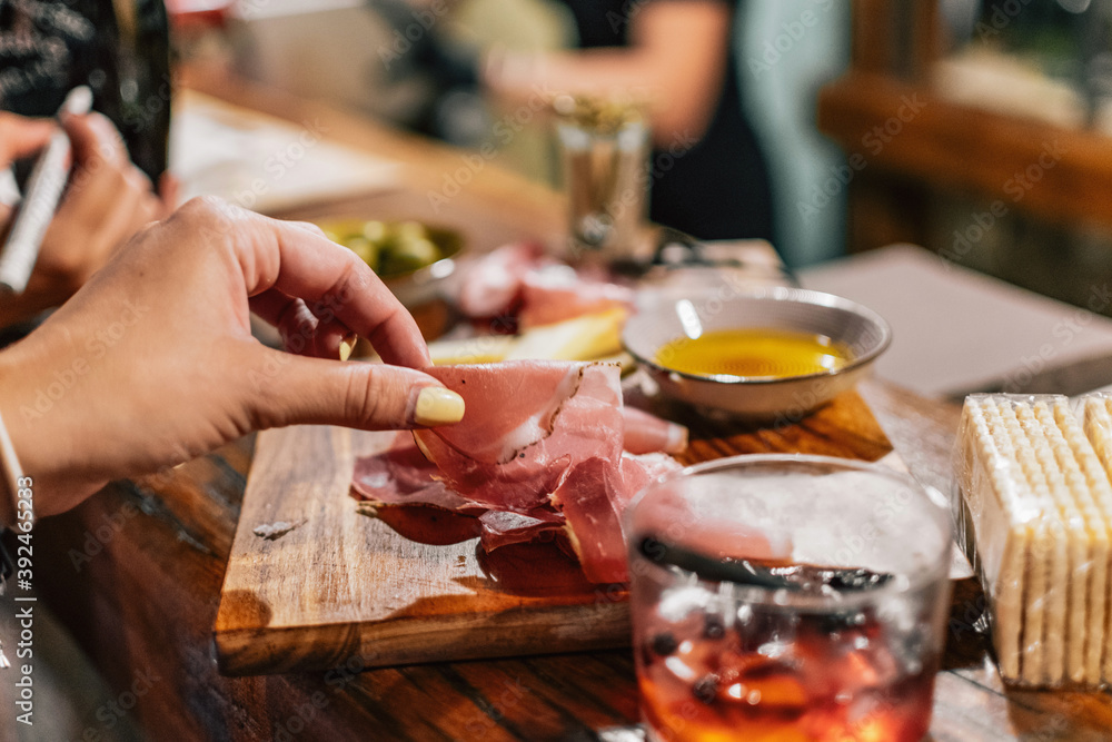 Female hand taking a piece of cured pork meat from a charcuterie board ...