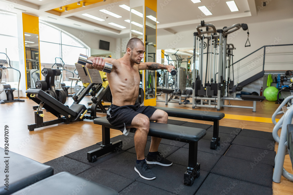 Handsome muscular bodybuilder man trains shoulder muscles by lifting ...