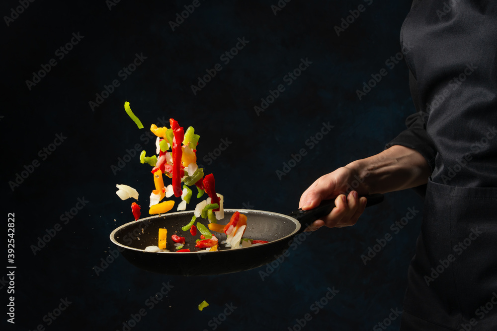 Chef hand throws up frying mix of colored vegetables above the pan on ...