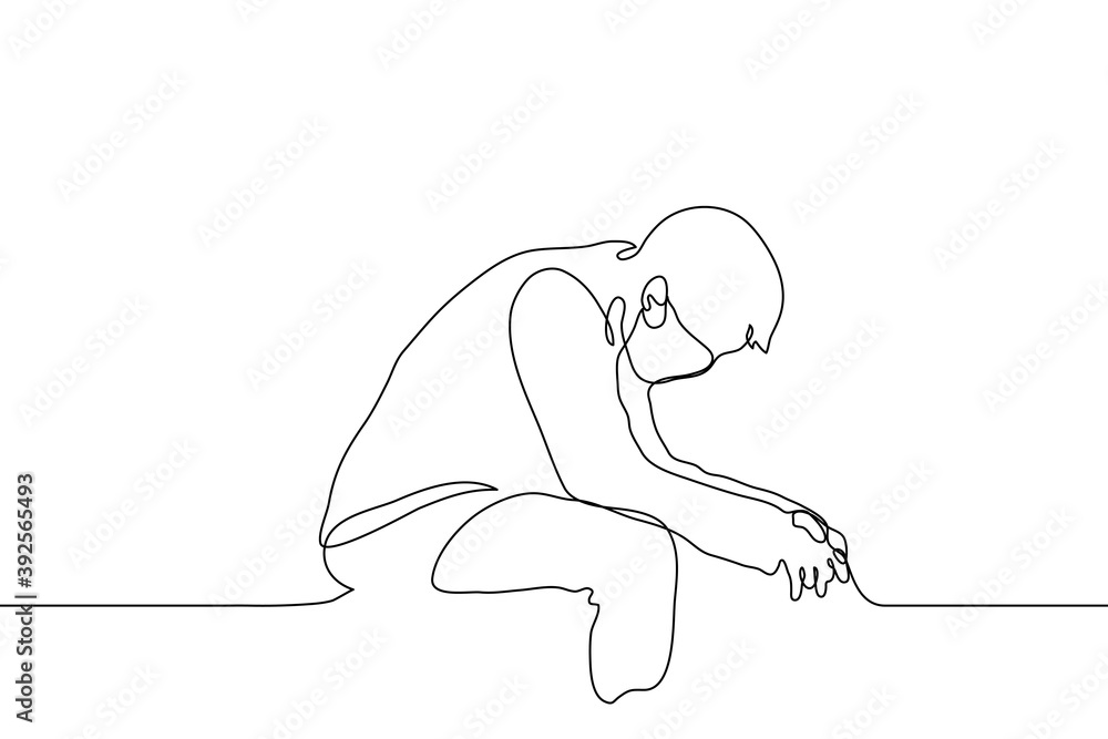 man sits in mask with his elbows on his knees, back is bent, head is down, hands are relaxed ...