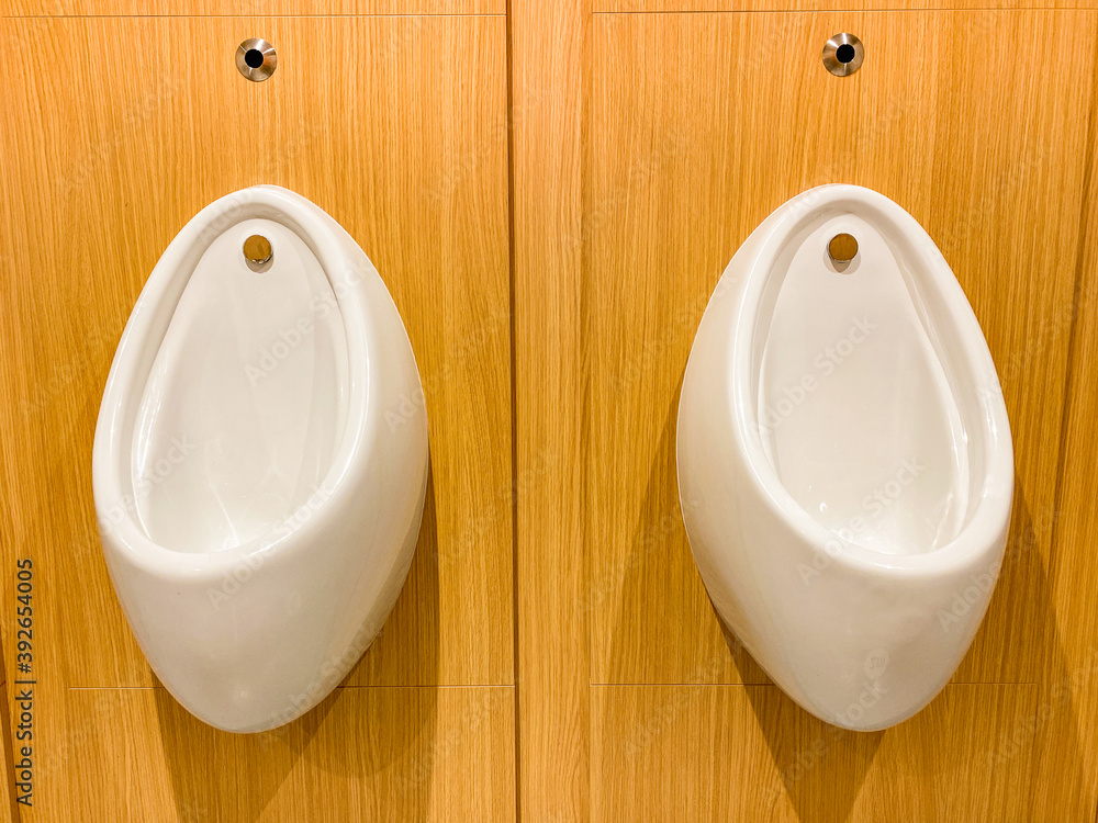 Two urinals in a male toilet fixed to wood panels on the wall. Above ...
