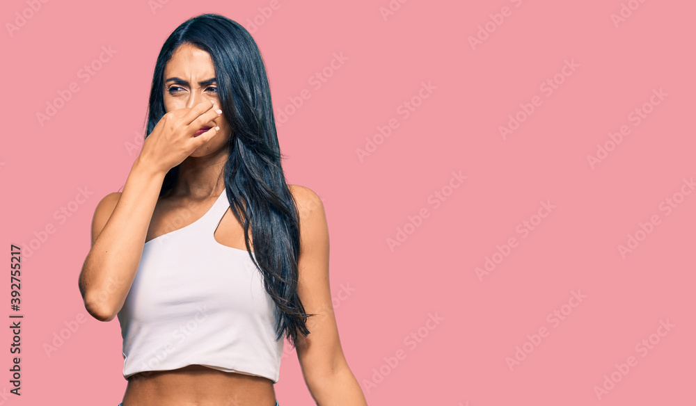Beautiful hispanic woman wearing casual clothes smelling something ...