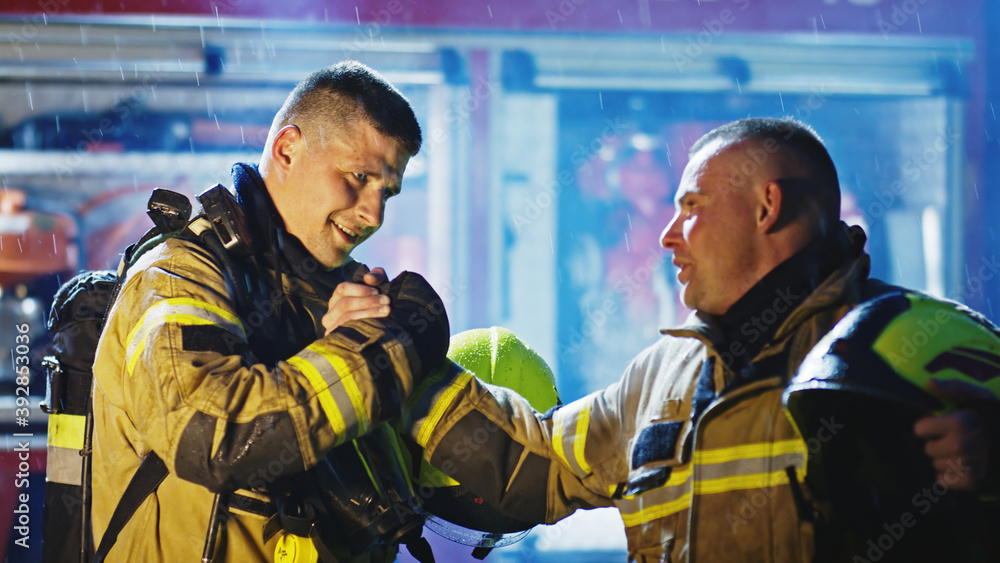Portrait of two young firefighters on the rain in front of fire engine ...